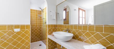 Casa de banho com paredes revestidas de azulejos amarelos, uma pia branca e um chuveiro.