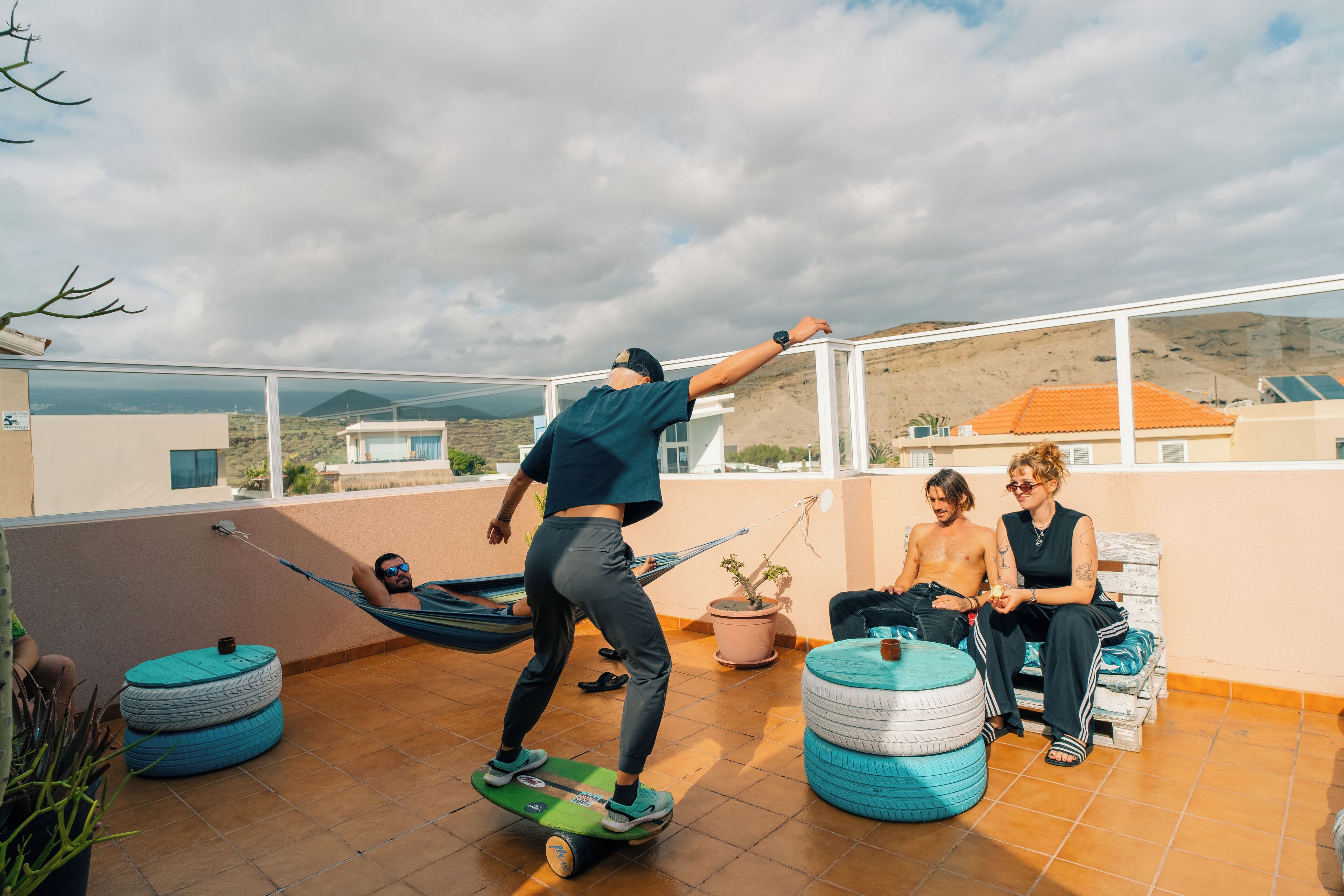 Terraço no telhado com uma pessoa de skate, outras sentadas e plantas em vasos.