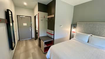 Quarto de hotel com cama, escrivaninha, guarda-roupa e espelho.