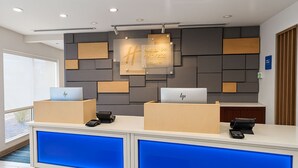 Balcão de recepção de hotel com duas estações de computador, design moderno na parede e uma janela visível.