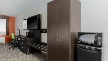 Quarto de hotel com um guarda-roupa grande, uma escrivaninha com cadeira, micro-ondas e televisão.