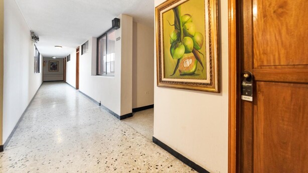 Um corredor com piso salpicado, um quadro emoldurado na parede e uma porta de madeira com fechadura.