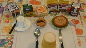 Uma mesa com diversos itens de comida, incluindo um bolo rotulado "Bacco", um pote de "Dolcinochoccolo" e uma xícara de café.