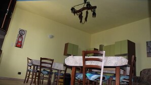 Uma área de refeições com cadeiras de madeira e uma mesa, um candelabro e um extintor de incêndio fixado na parede.