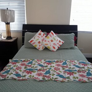 Uma cama com colcha florida, duas almofadas com estampas de peixe e um abajur em uma mesa de cabeceira.