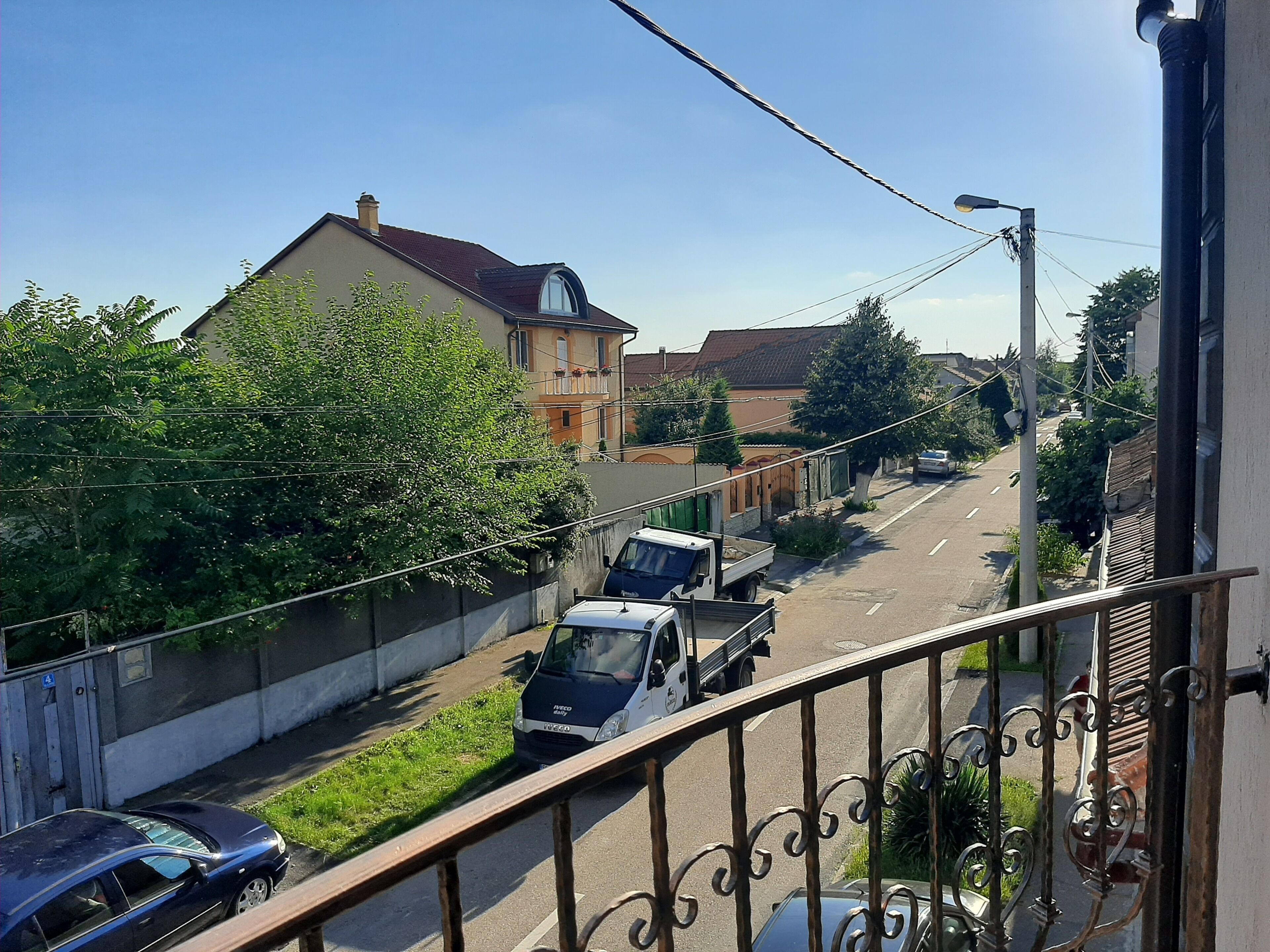 Rua residencial com casas, carros estacionados e céu claro.