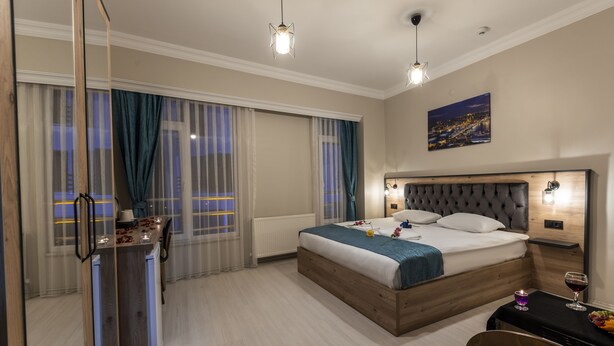 Quarto de hotel moderno com cama grande, mesas de cabeceira, escrivaninha e uma janela ampla com cortinas.