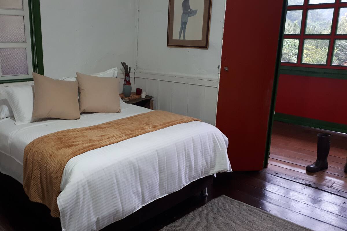 Quarto com cama, almofadas, mesa de cabeceira, um vaso e um quadro na parede.
