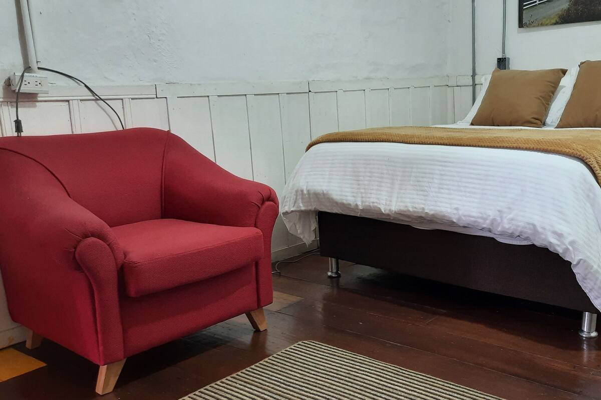 Quarto com uma cama, uma poltrona vermelha e um radiador.