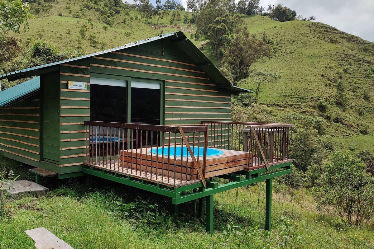 Uma cabana pequena com telhado verde, deck de madeira e piscina.