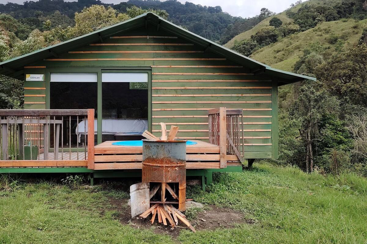 Uma pequena cabana de madeira com telhado verde, um deque de madeira e um portão de metal.