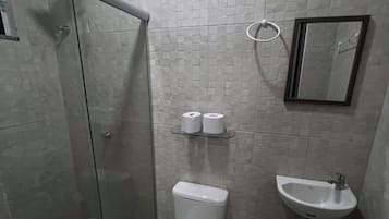 Casa de banho com cabine de duche em vidro, sanita, lavatório e espelho.