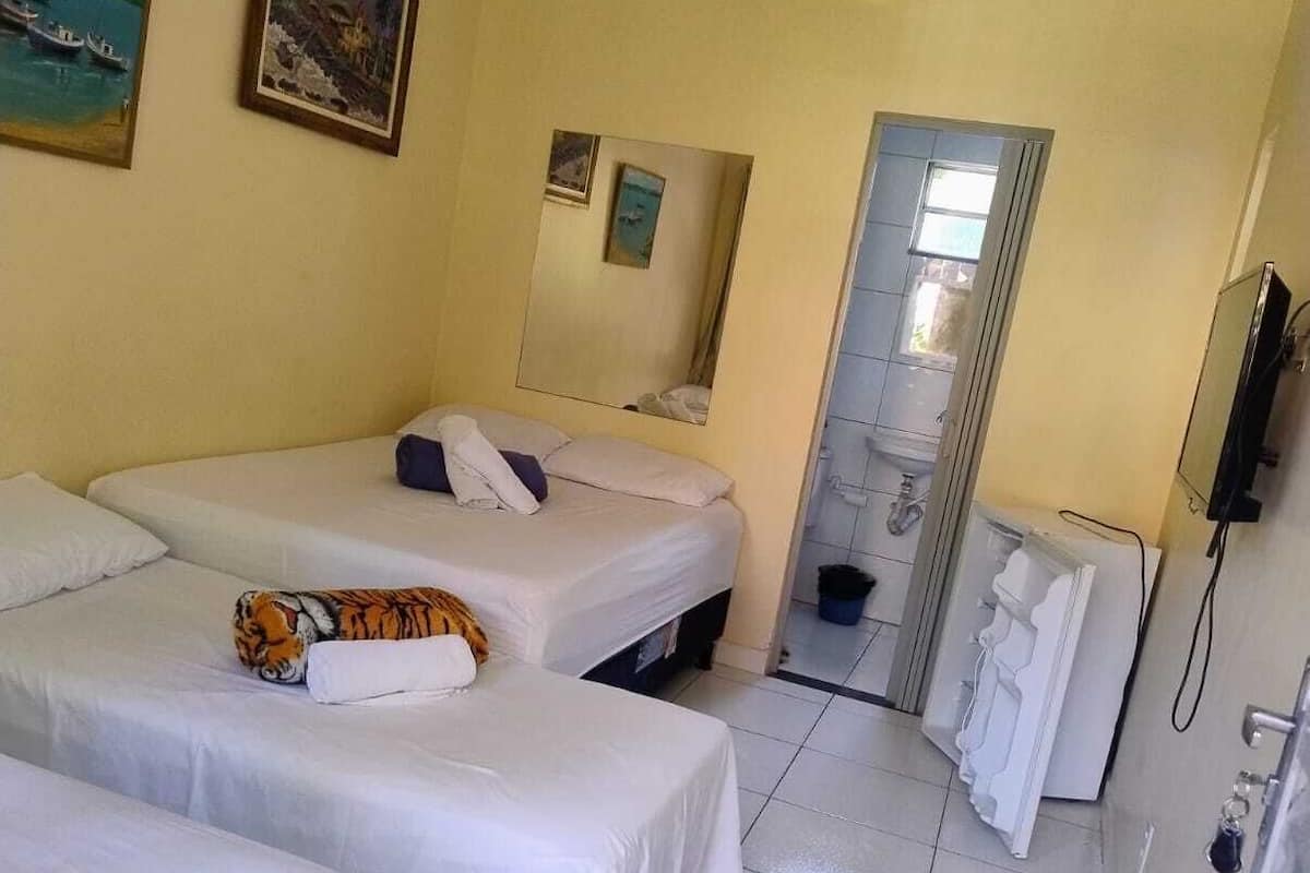 Quarto de hotel com duas camas, banheiro com chuveiro e televisão.