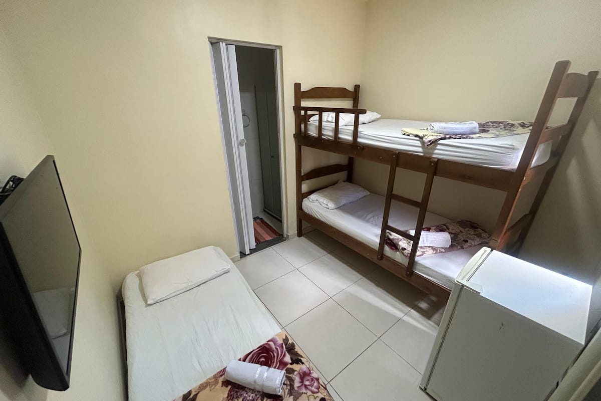 Um dormitório com beliches, uma cama de solteiro, uma mesa e uma porta que dá para um banheiro.