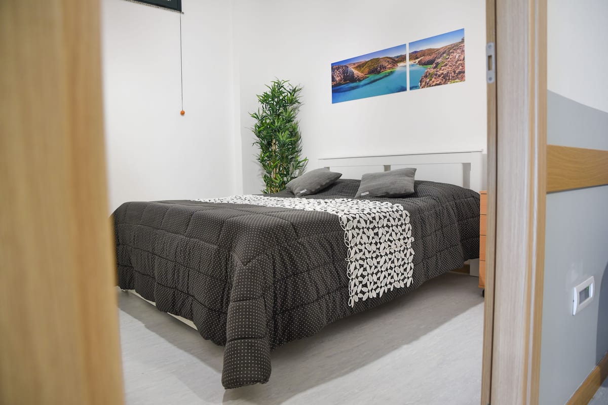 Quarto com cama, planta na mesa de cabeceira e quadro na parede.