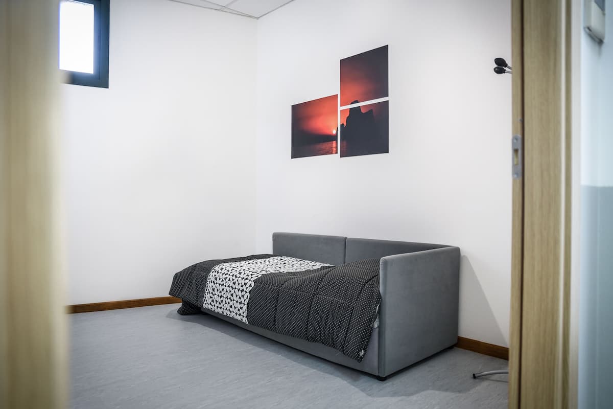 Quarto moderno com sofá cinza, manta estampada e obra de arte na parede retratando um pôr do sol.