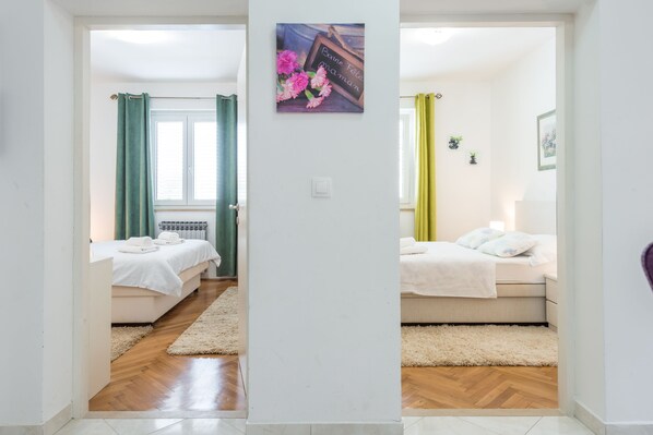 Quarto de hotel com duas camas, uma janela com cortinas, uma parede branca e um quadro sobre a cama.