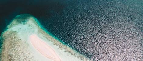 Vista aérea de uma ilha tropical com águas turquesa cristalinas, uma praia de areia e um pequeno povoado.