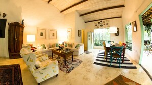 Uma sala de estar espaçosa com teto alto, um espaço para refeições com um tapete listrado e vista para o verde lá fora.