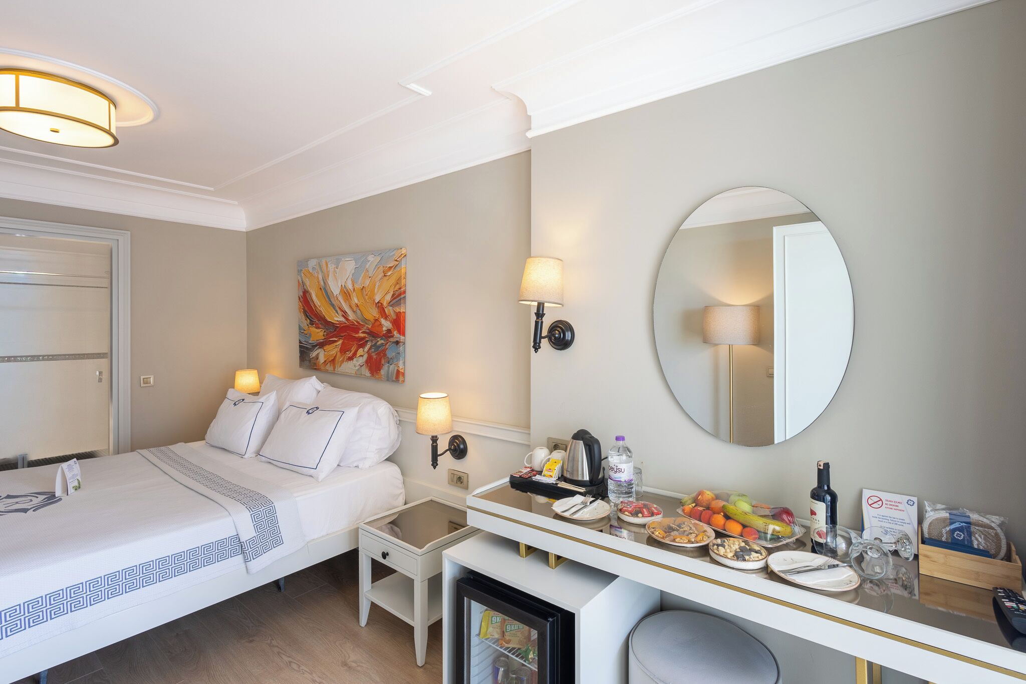 Quarto de hotel com duas camas, uma mesa pequena com abajur, um refrigerador e um balcão com comida e bebidas.
