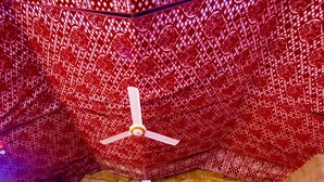 Quarto com dossel vermelho estampado, ventilador de teto, duas áreas de estar acolchoadas e uma parede de pedra.