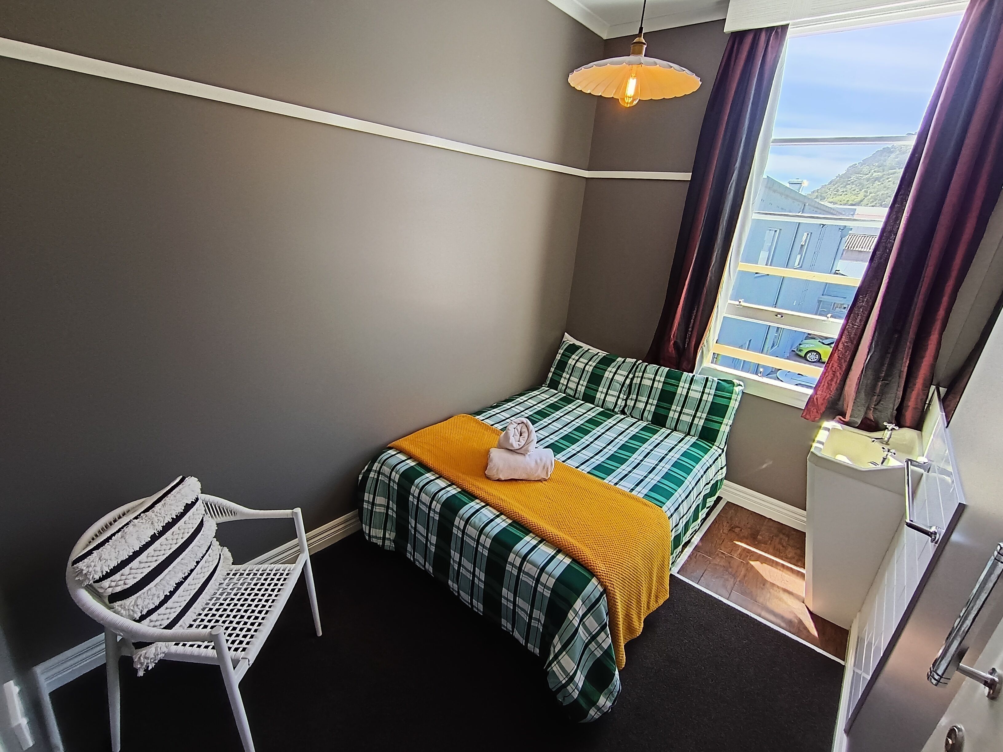 Quarto com cama, cadeira, janela com cortinas e luminária suspensa.