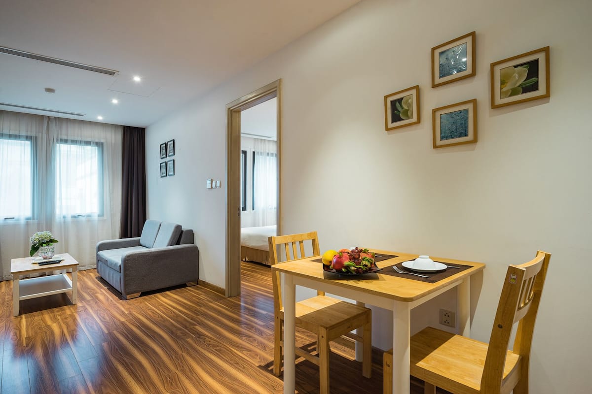 Uma sala de estar moderna com sofá, mesa de jantar com cadeiras e uma pequena mesa lateral com uma planta.