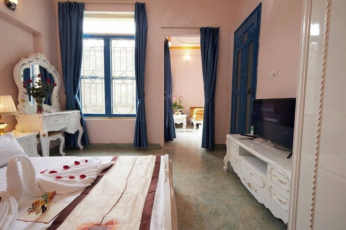 Quarto de hotel com cama, televisão, penteadeira, espelho e janela com cortinas.