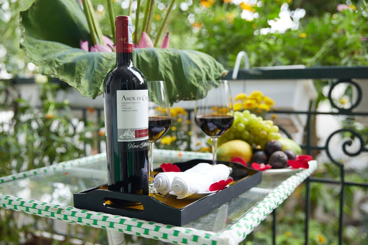 Uma garrafa de vinho sobre uma mesa de vidro, com uma bandeja de uvas e uma toalha enrolada.