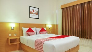 Quarto de hotel com cama de madeira, roupa de cama branca, almofadas vermelhas, duas mesas de cabeceira com abajures e um quadro na parede.