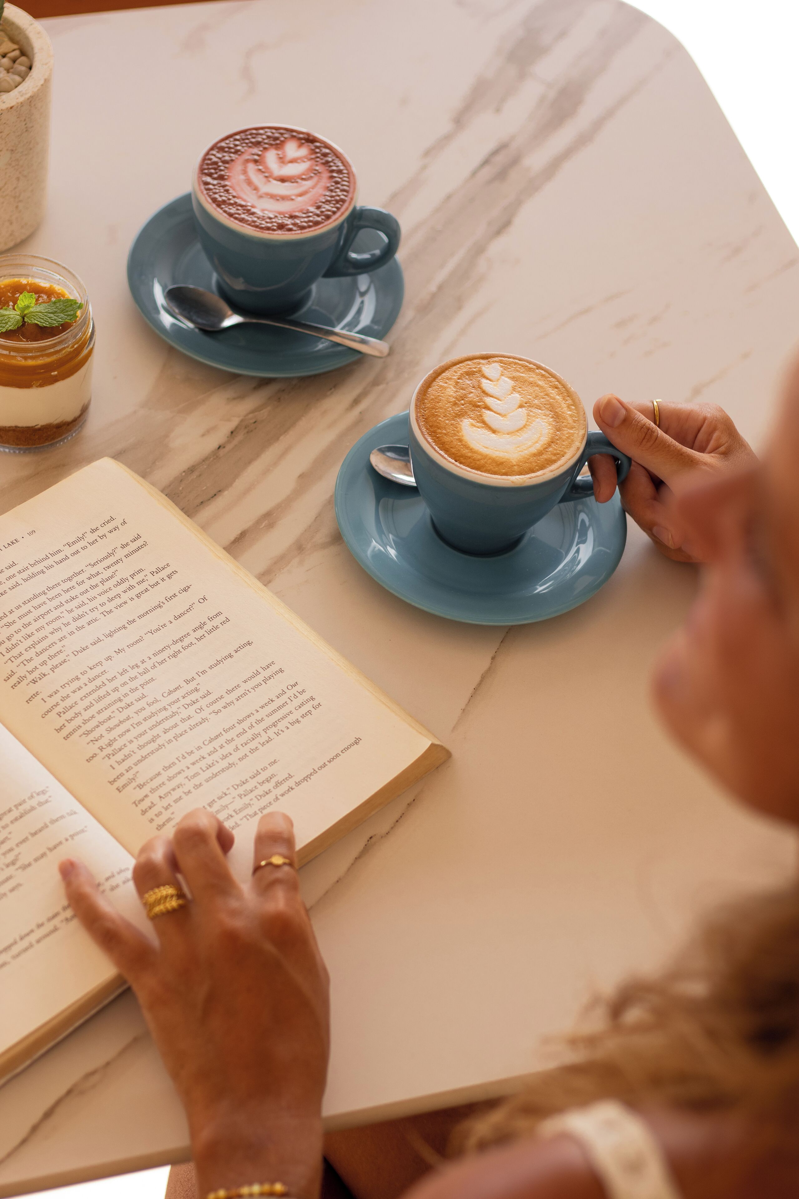Uma pessoa lendo um livro com uma xícara de café sobre uma mesa de mármore.