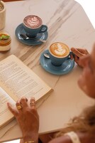 Uma pessoa lendo um livro com uma xícara de café sobre uma mesa de mármore.