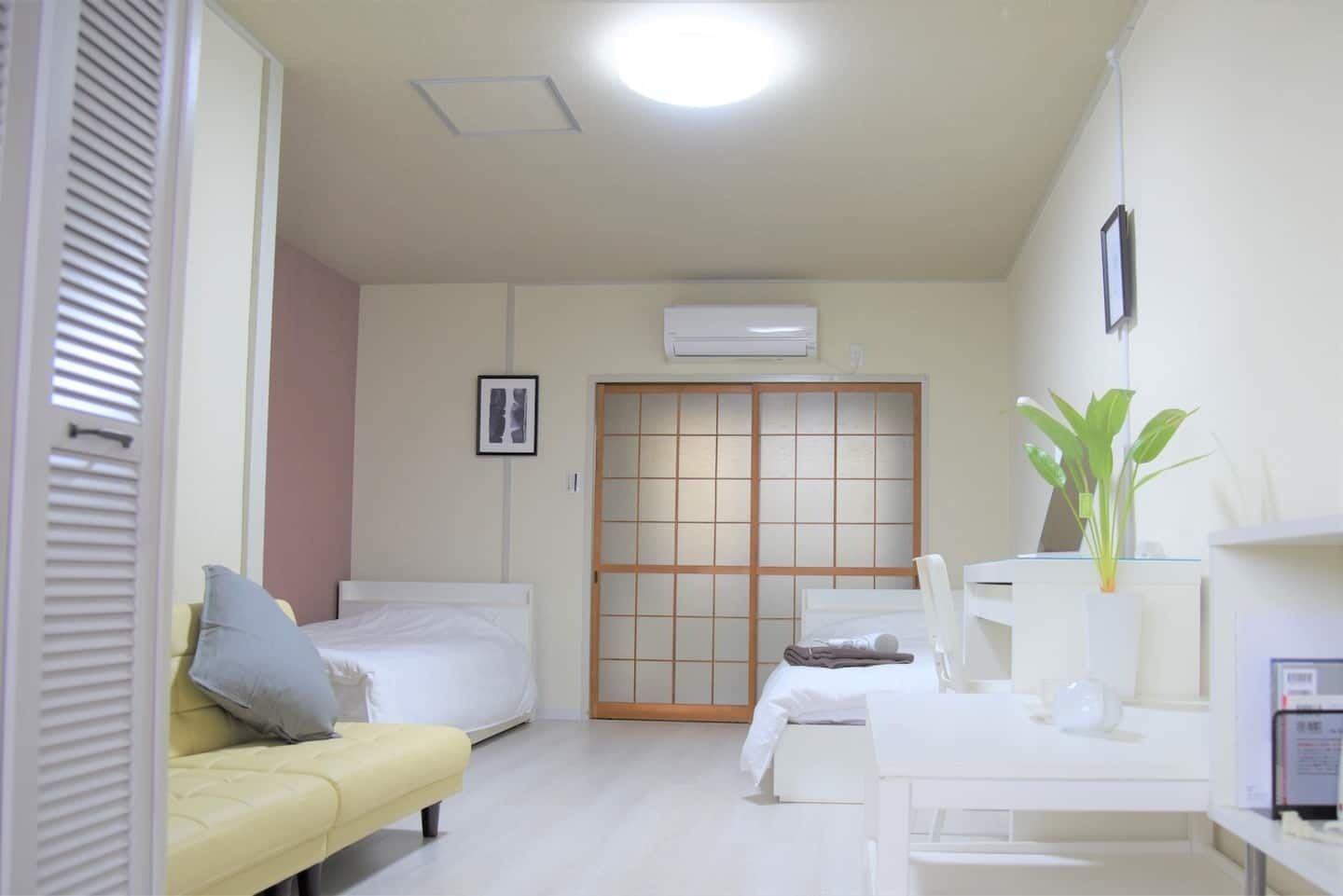 Quarto de hotel compacto com cama, sofá, mesinha e porta deslizante.
