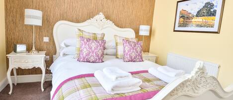 Cama bem arrumada com colcha xadrez e almofadas decorativas, mesa de cabeceira com abajur e um quadro na parede.