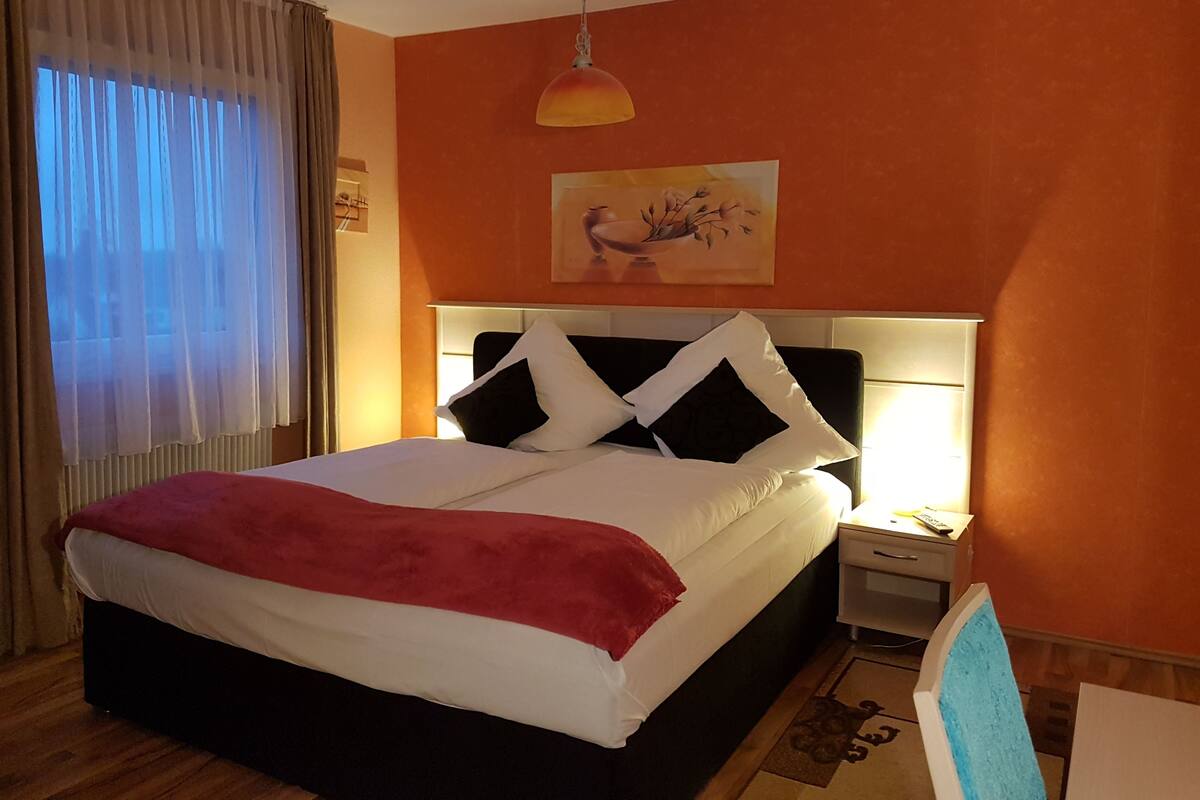 Quarto de hotel com cama, mesa de cabeceira, escrivaninha e cadeira.