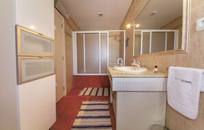 Casa de banho com chuveiro, lavatório e espelho.