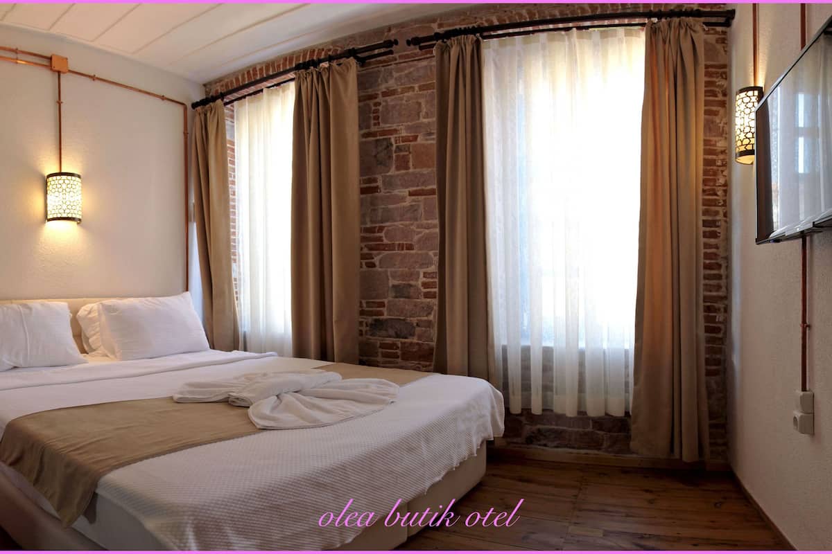 Quarto de hotel com cama, TV na parede e janela com cortinas.
