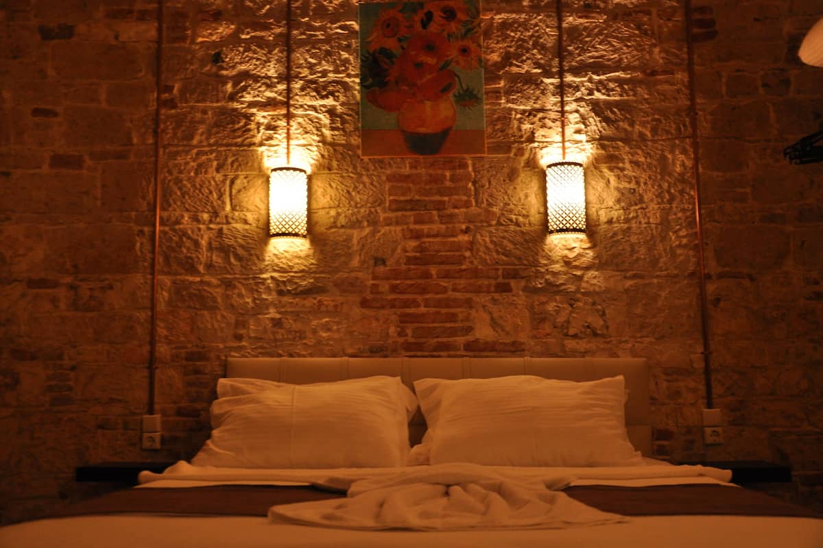 Quarto com parede de tijolos, duas luminárias fixadas na parede e um quadro de flores sobre a cama com roupa de cama branca.