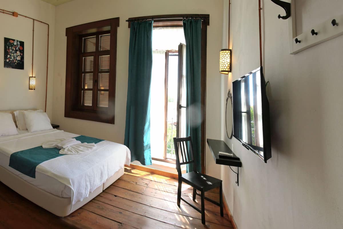 Quarto com cama, duas luminárias na parede, televisão e janela com cortinas.