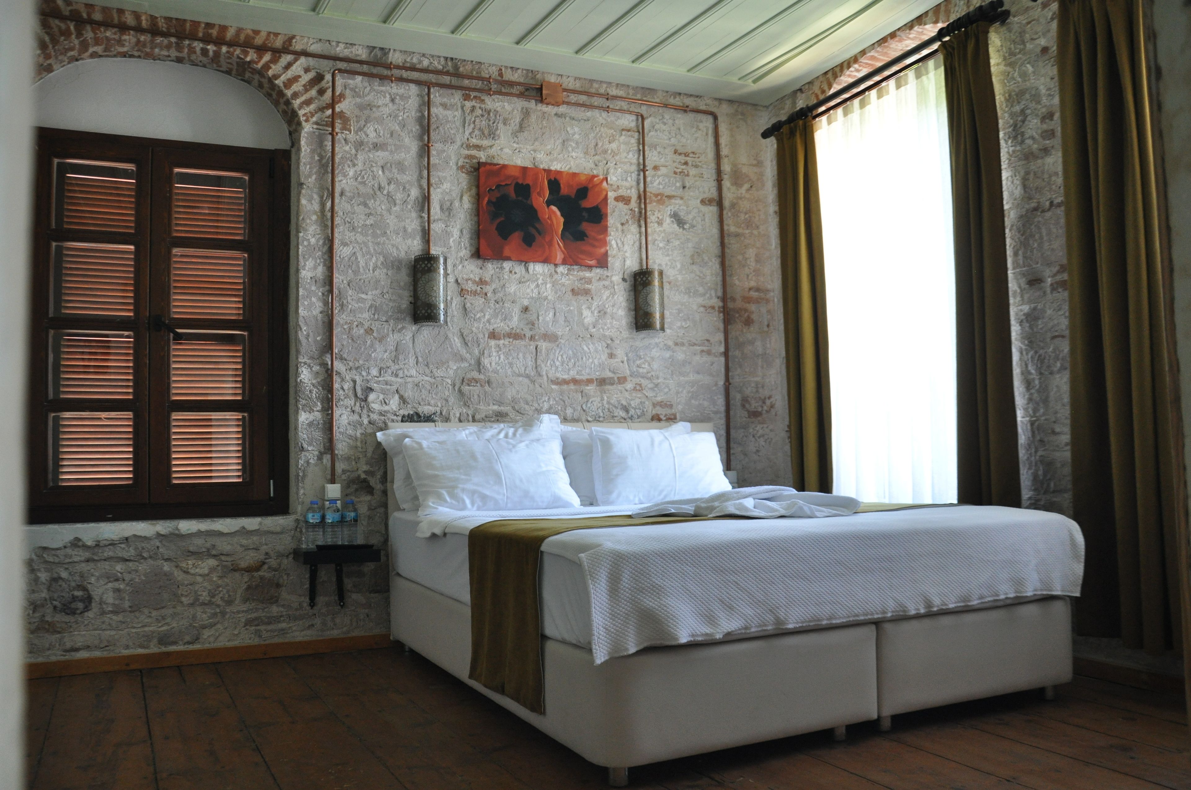 Quarto com uma cama grande, paredes de pedra, porta de madeira e janela com cortinas.