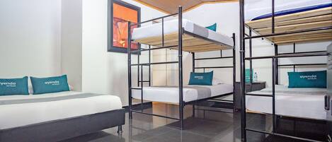 Quarto de hotel com beliches, teto de madeira, quadro na parede e uma cama com travesseiro da marca "ayenda hotels".