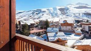 Uma cidadezinha montanhosa coberta de neve, com edifícios de madeira e uma vista desobstruída das montanhas.