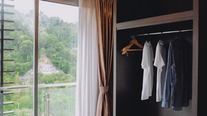 Quarto com uma janela grande, cortina e um cabideiro com roupas penduradas.