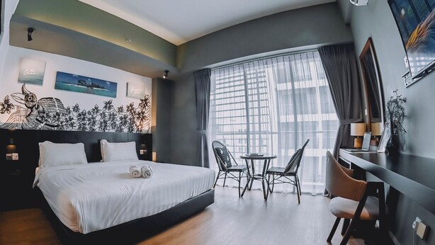 Quarto de hotel moderno com uma cama grande, uma mesa com duas cadeiras, uma janela ampla com cortinas e obras de arte nas paredes.