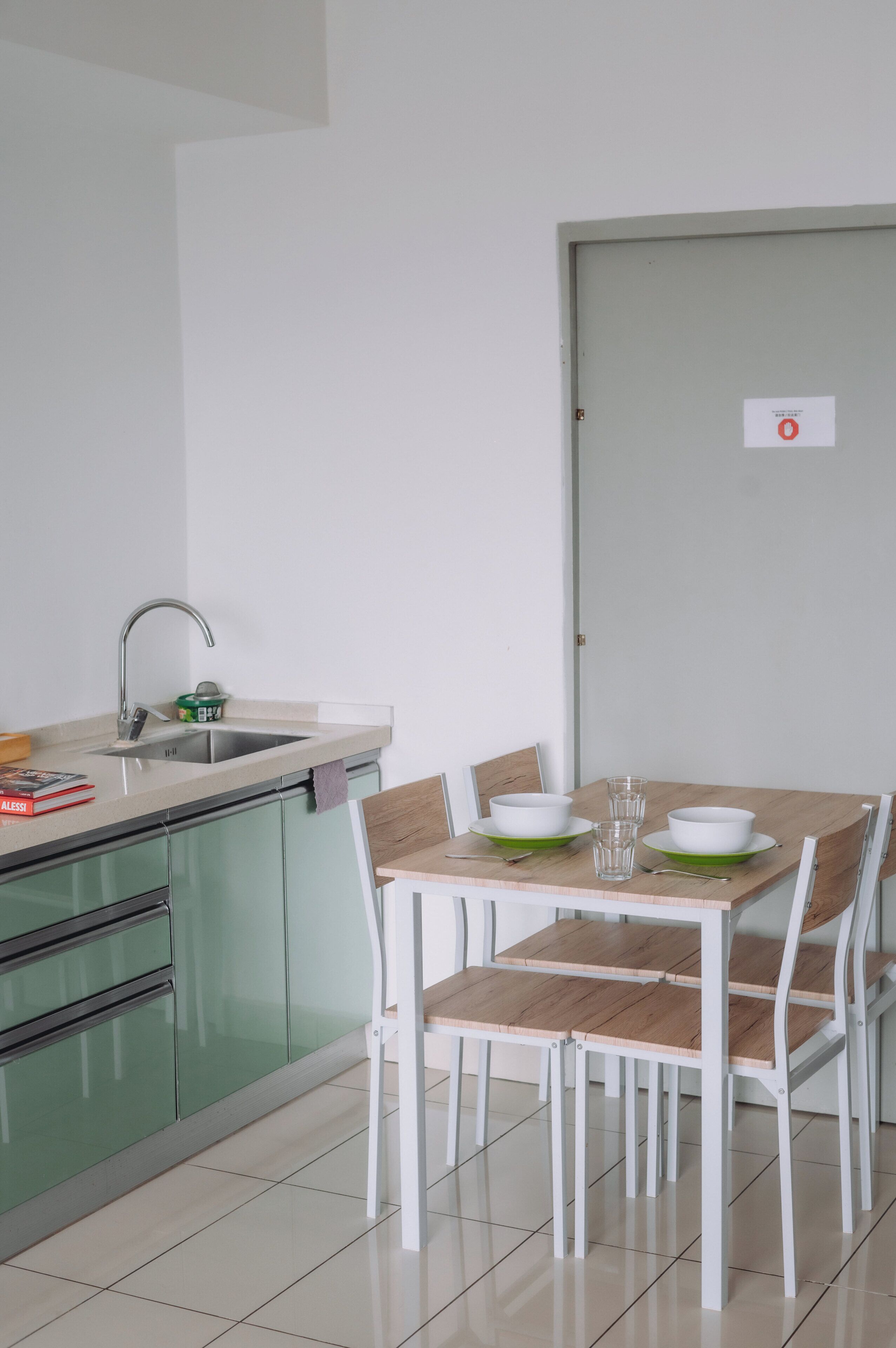 Uma cozinha com pia, mesa e cadeiras, e uma porta com placa.