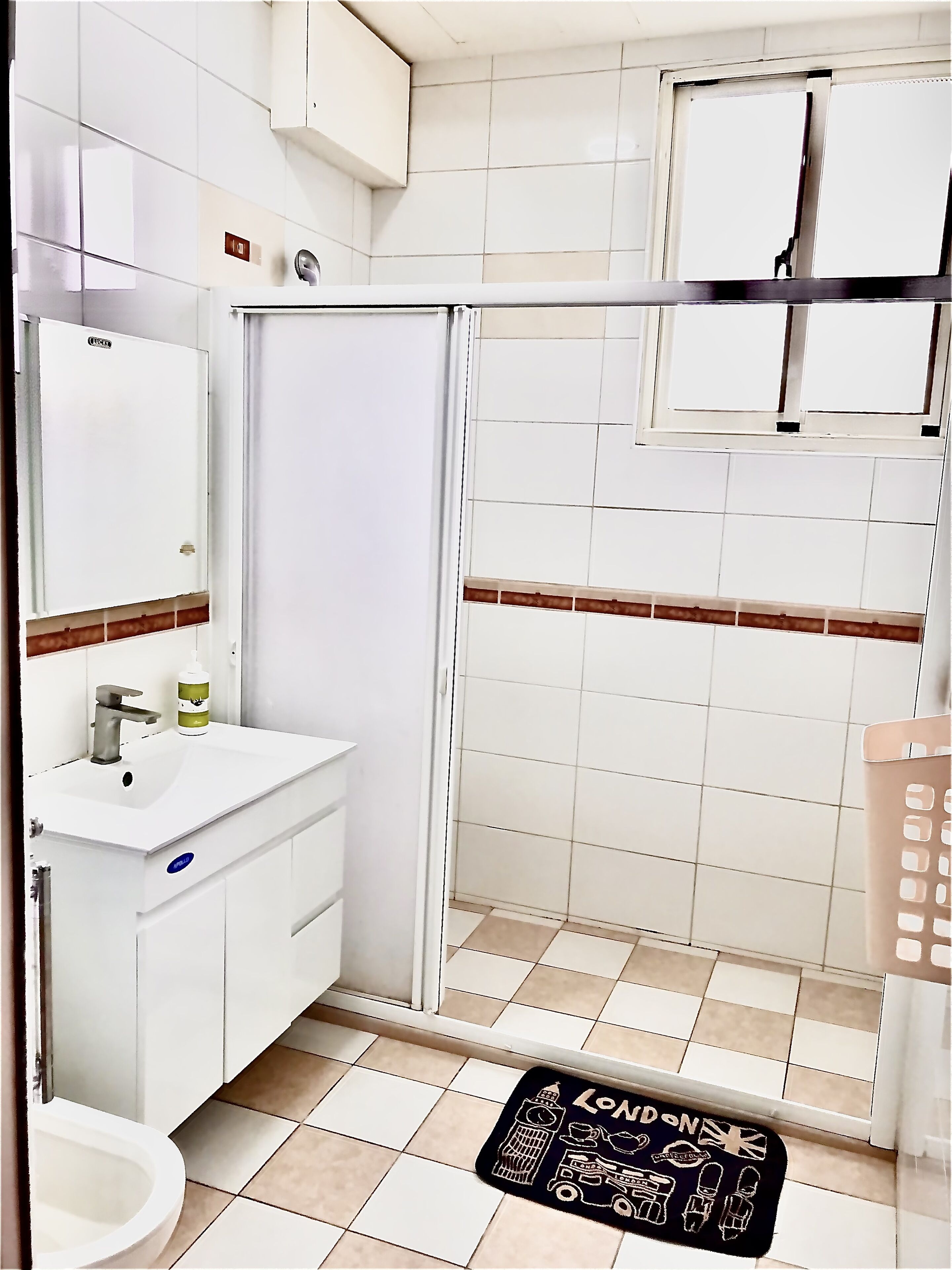 Casa de banho com lavatório branco, espelho e armário, sanita e área de duche com chão em mosaico.
