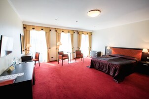 Quarto de hotel com uma cama grande, uma escrivaninha com cadeira, uma pequena mesa com duas cadeiras e um armário.