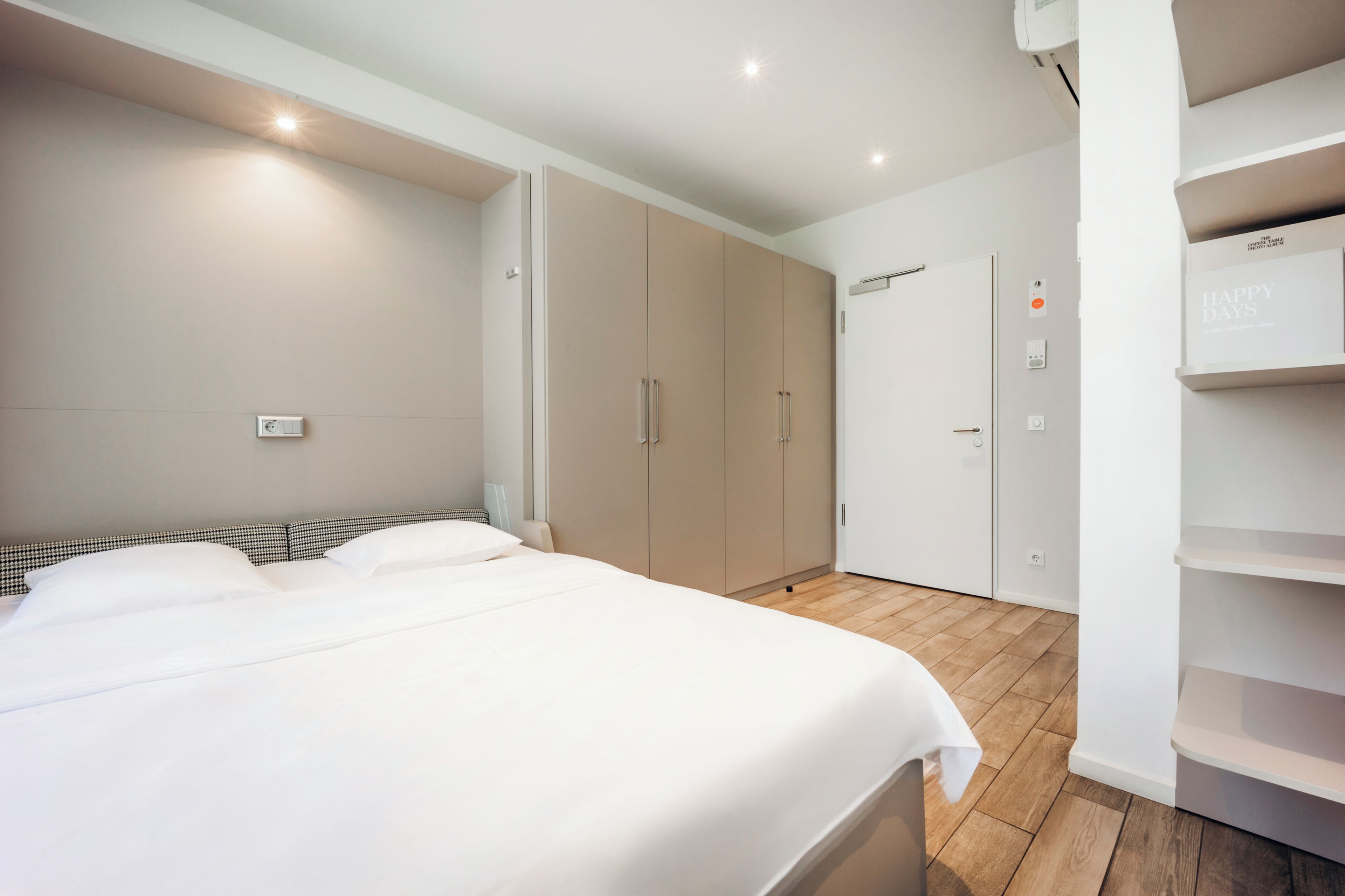 Quarto de hotel moderno com uma cama grande, um guarda-roupa e uma estante embutida.