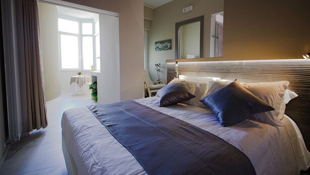 Quarto com cama grande, mesa de cabeceira, espelho e janela com cortinas.