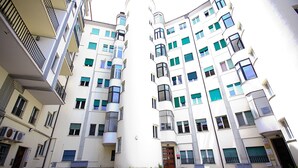 Edifício residencial de vários andares com varandas, pátio central e entrada no nível da rua.